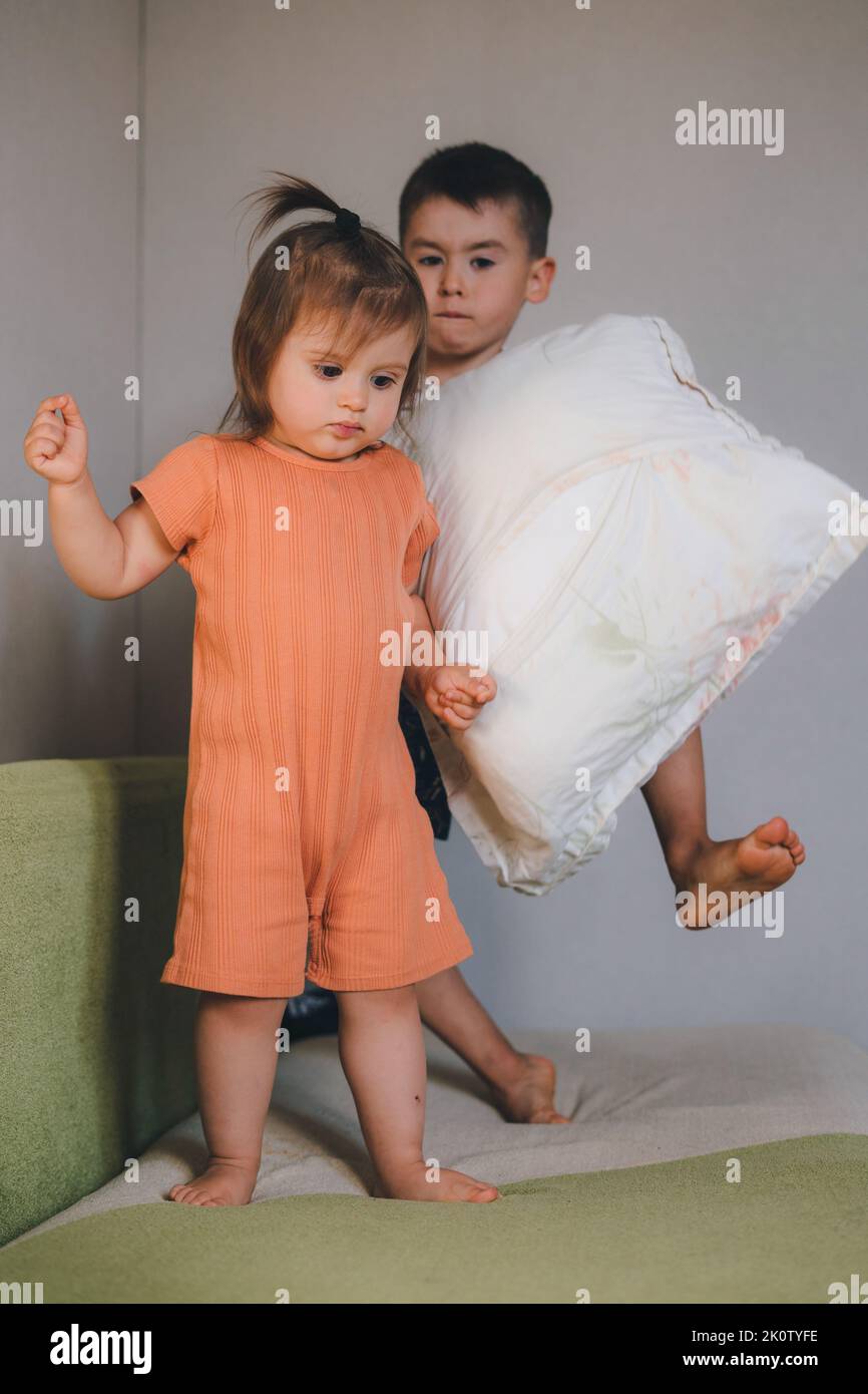 Happy cheerful boy playing in living room with his baby sister throwing ...