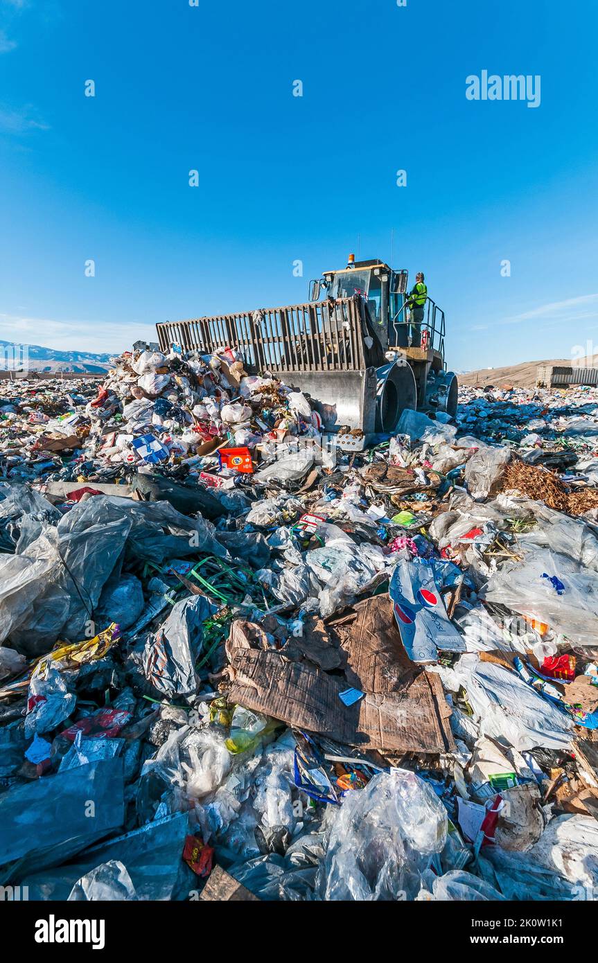 A soil compactor bulldozer pushing solid waste at an active landfill ...
