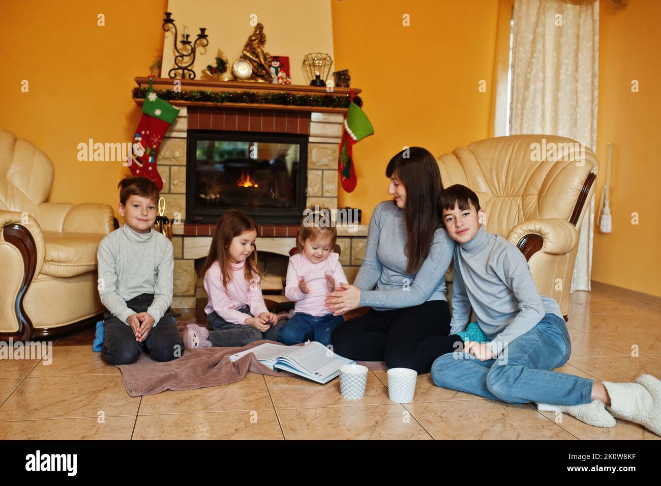 Happy young large family by a fireplace in warm living room on winter ...