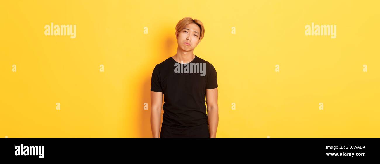 Portrait of exhausted and sad asian guy looking sad, standing drained ...