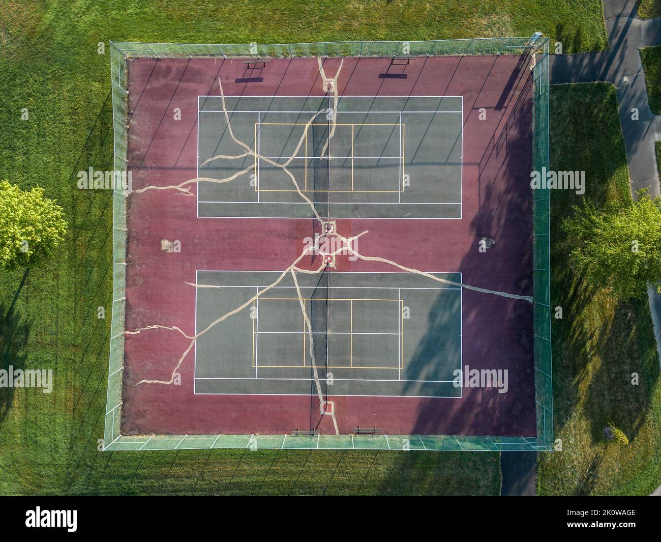 An aerial top view of a tennis court surrounded by green grass on a ...