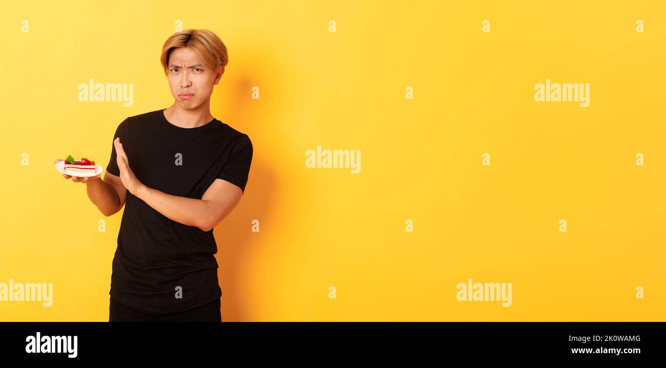 Portrait of disgusted and upset young asian guy refuse eating cake ...
