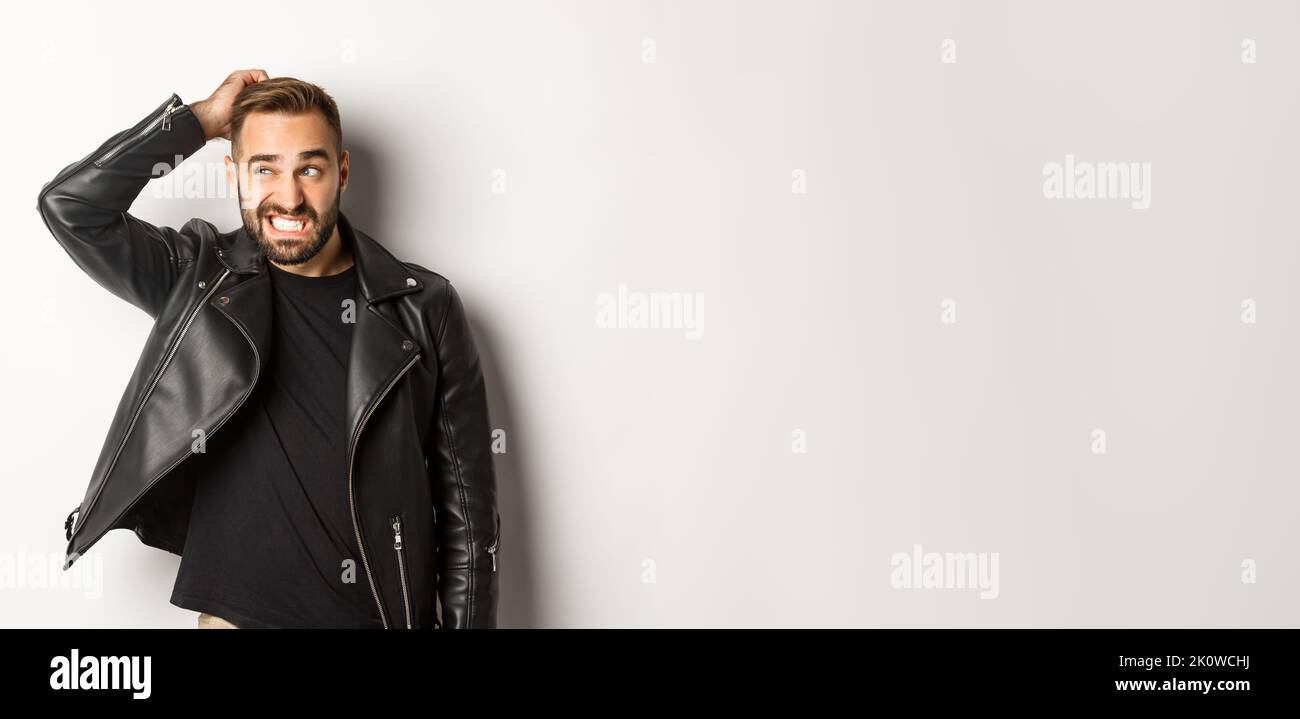 Confused macho guy in black leather jacket looking awkward and unsure ...