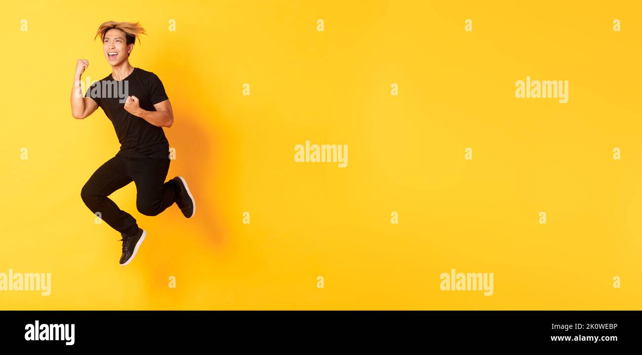 Full-length of happy attractive asian guy in black clothes jumping and ...