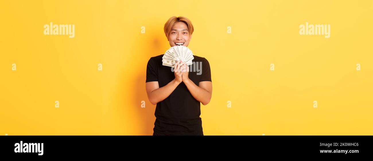 Cheerful winning handsome asian guy, smiling pleased and holding money ...