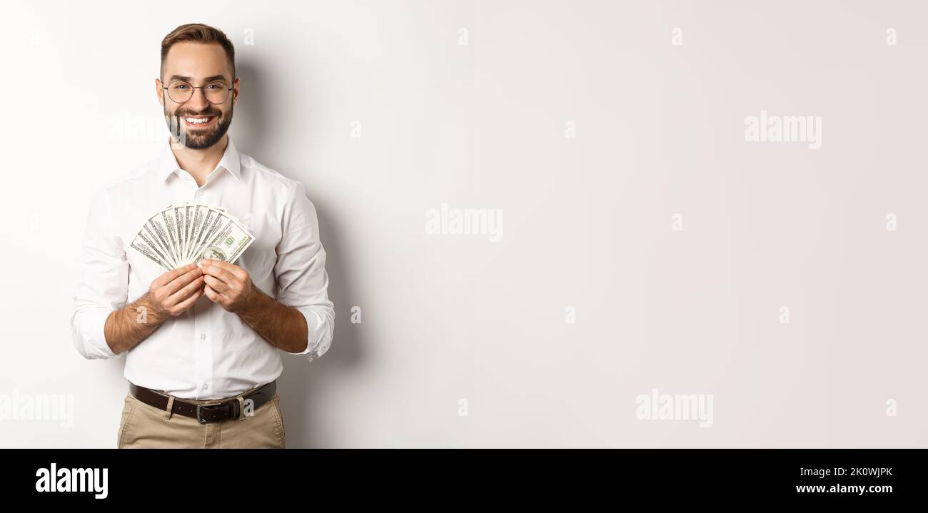 Smiling handsome man holding money, showing dollars, standing over ...
