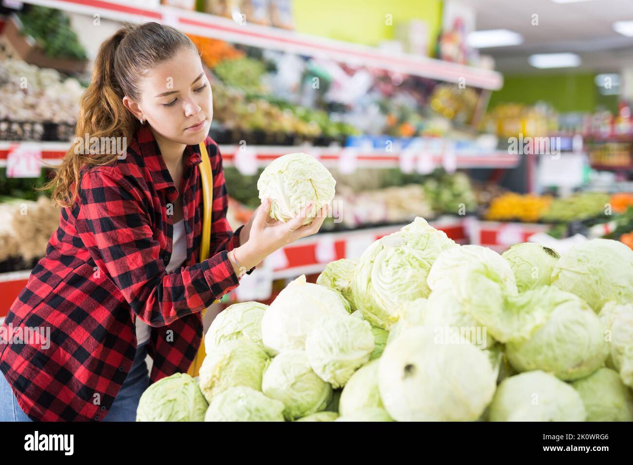 Positive customer chooses cabbages at grocery store Stock Photo - Alamy