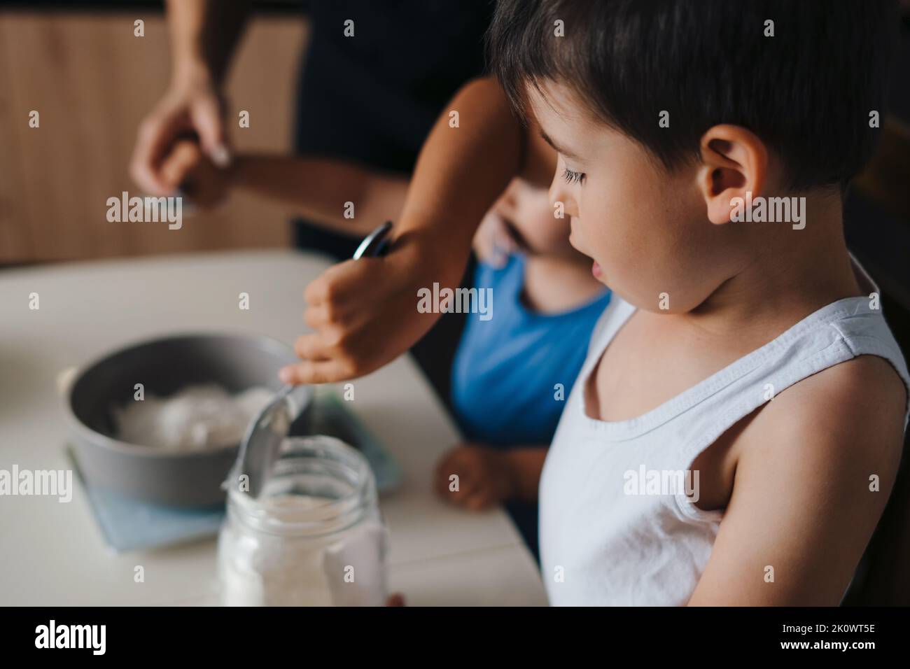 Cute little baby girl adding ingredients to bowl while preparing dough ...