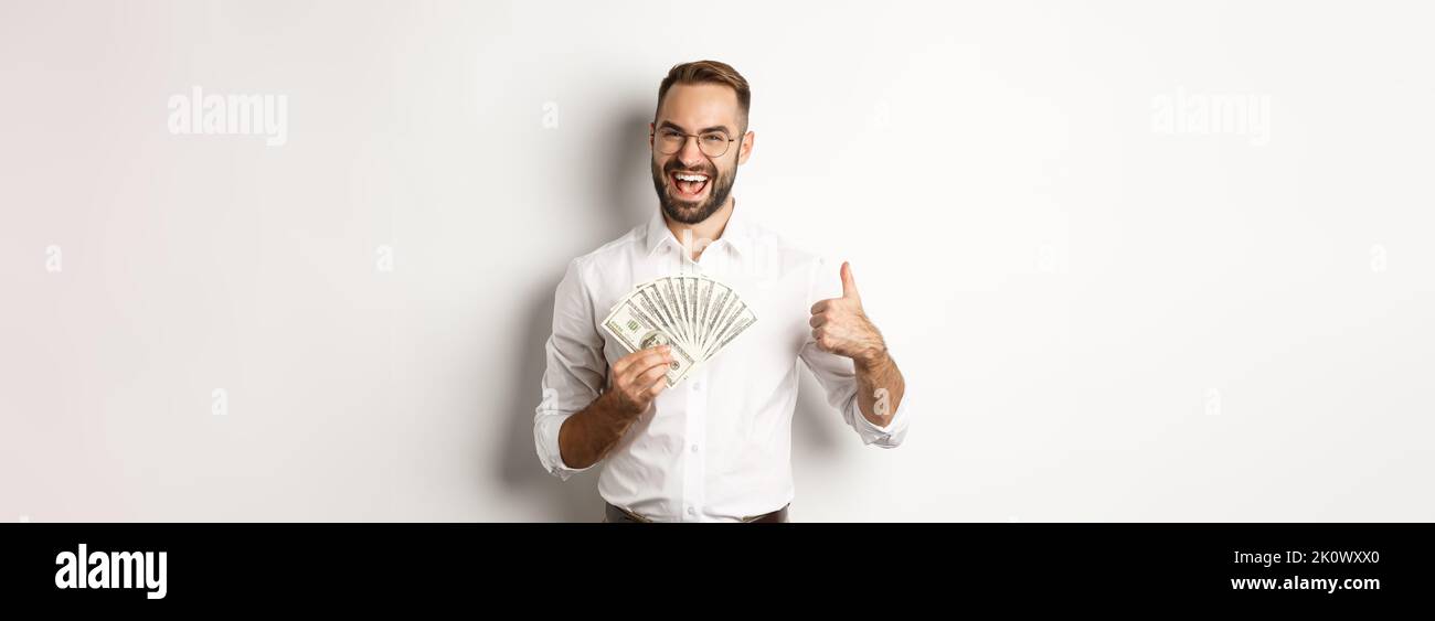 Excited rich man holding money, showing thumb up in approval, standing ...