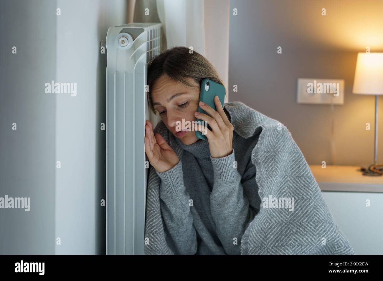 Young woman leaning on heating radiator talks on phone with hotline to ...