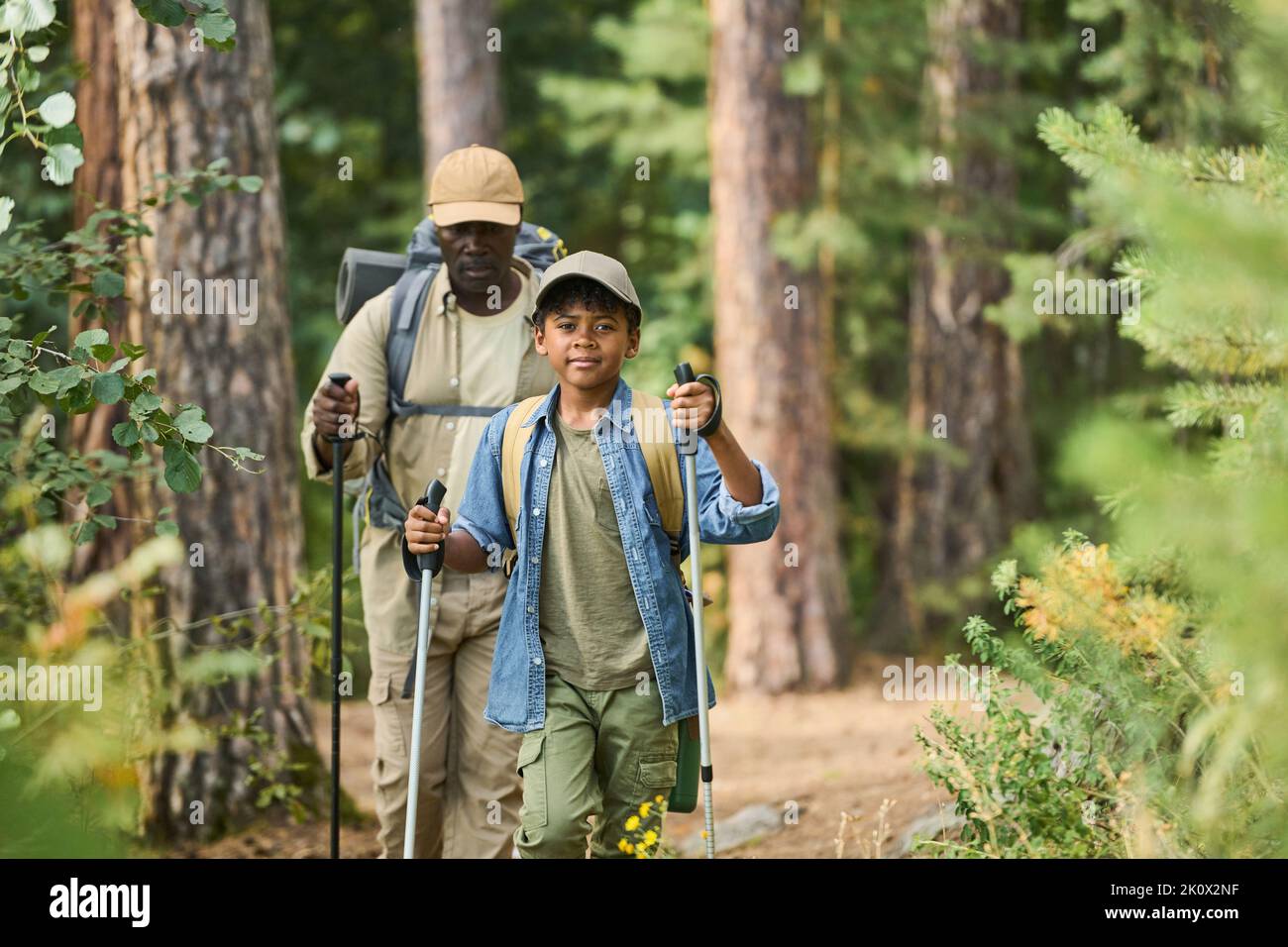 Cute little boy with trekking sticks moving down long narrow footpath ...