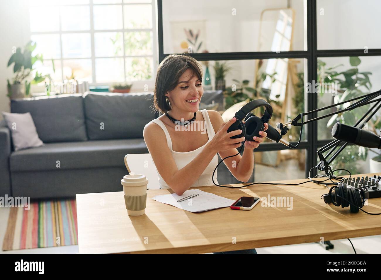 Young smiling female host putting on headphones while sitting by ...