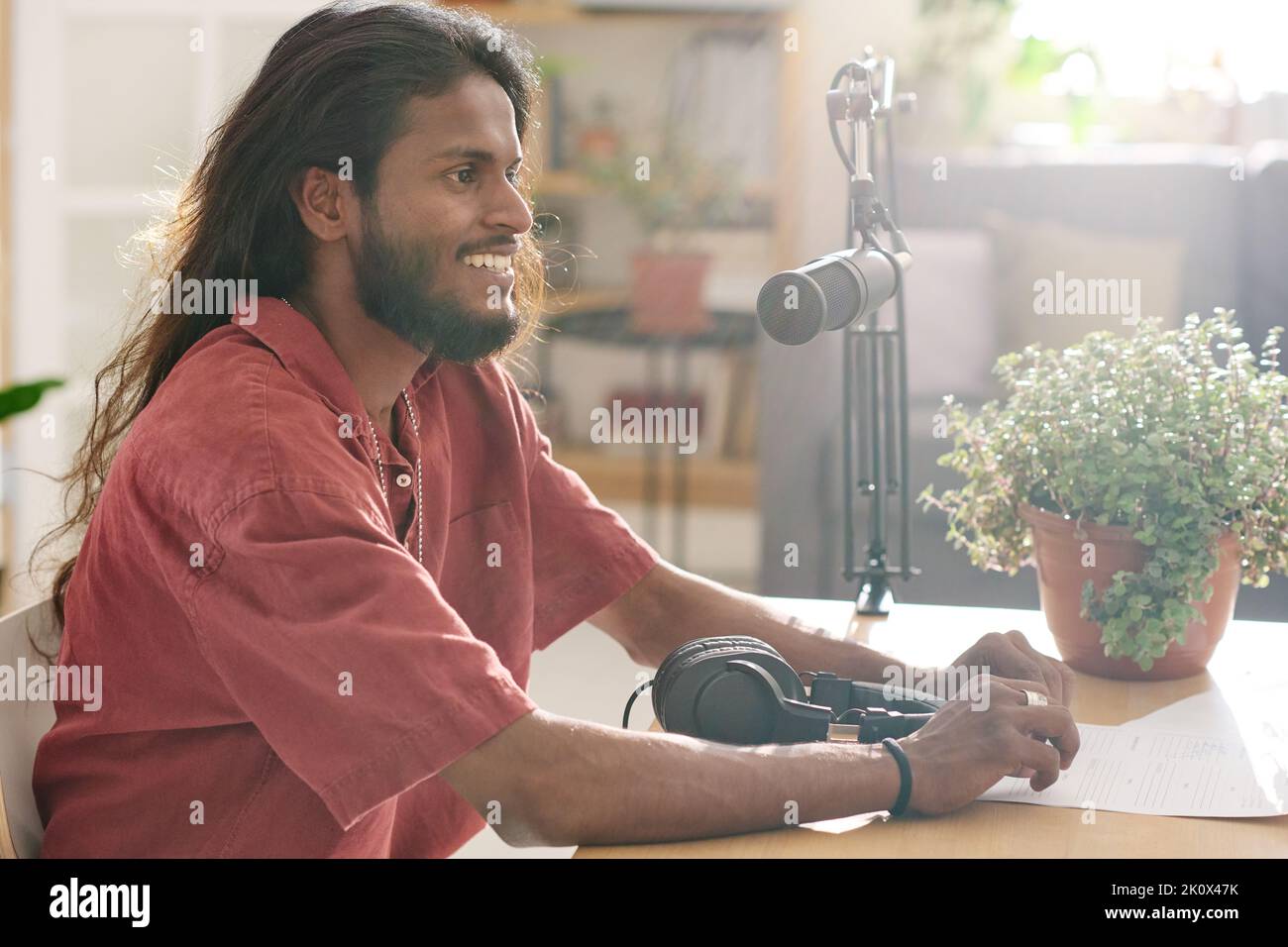 SIde view of young male host sitting in front of microphone by desk and ...