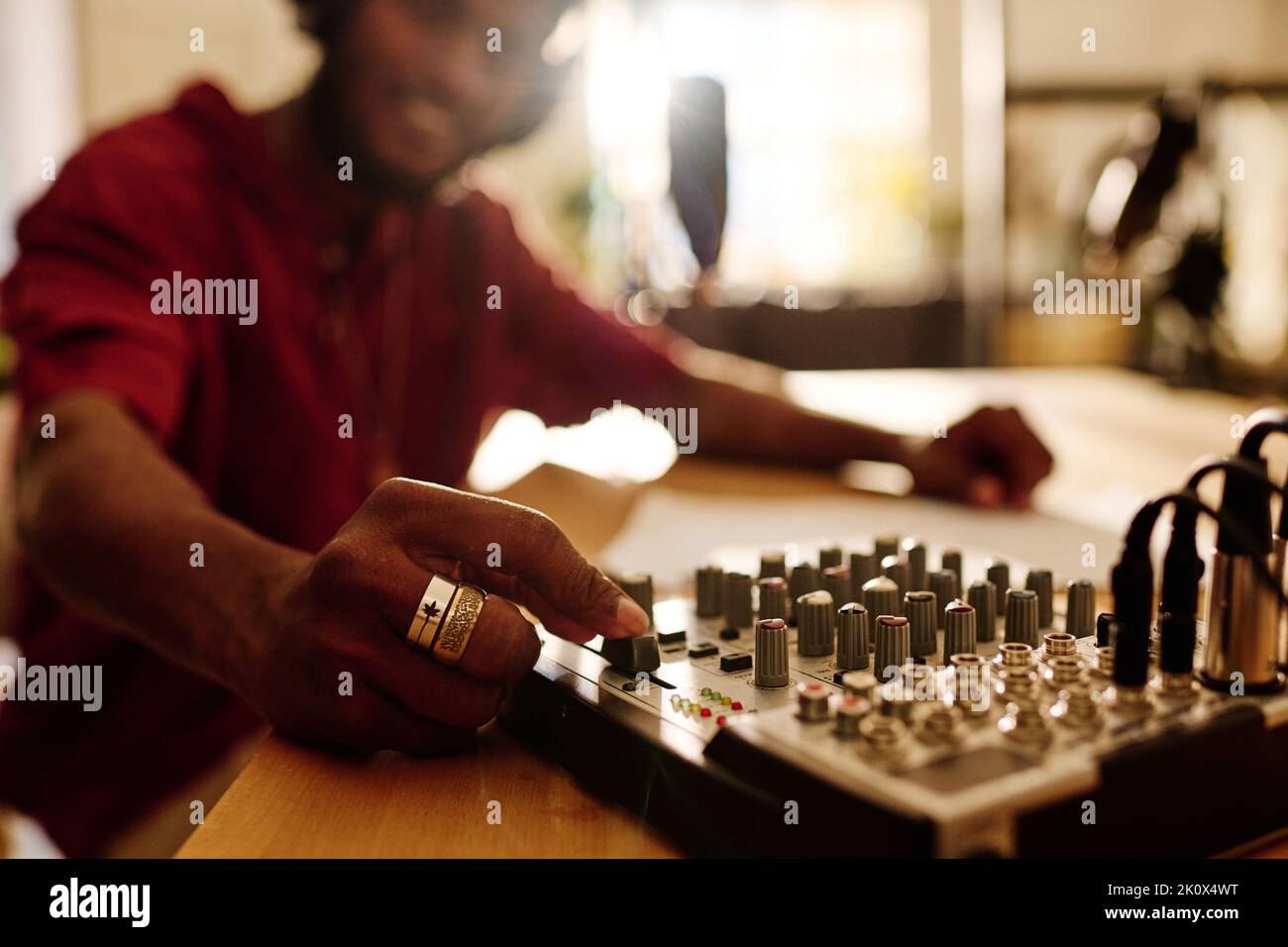 Hand of young man rotating mixer console while sitting by workplace in ...