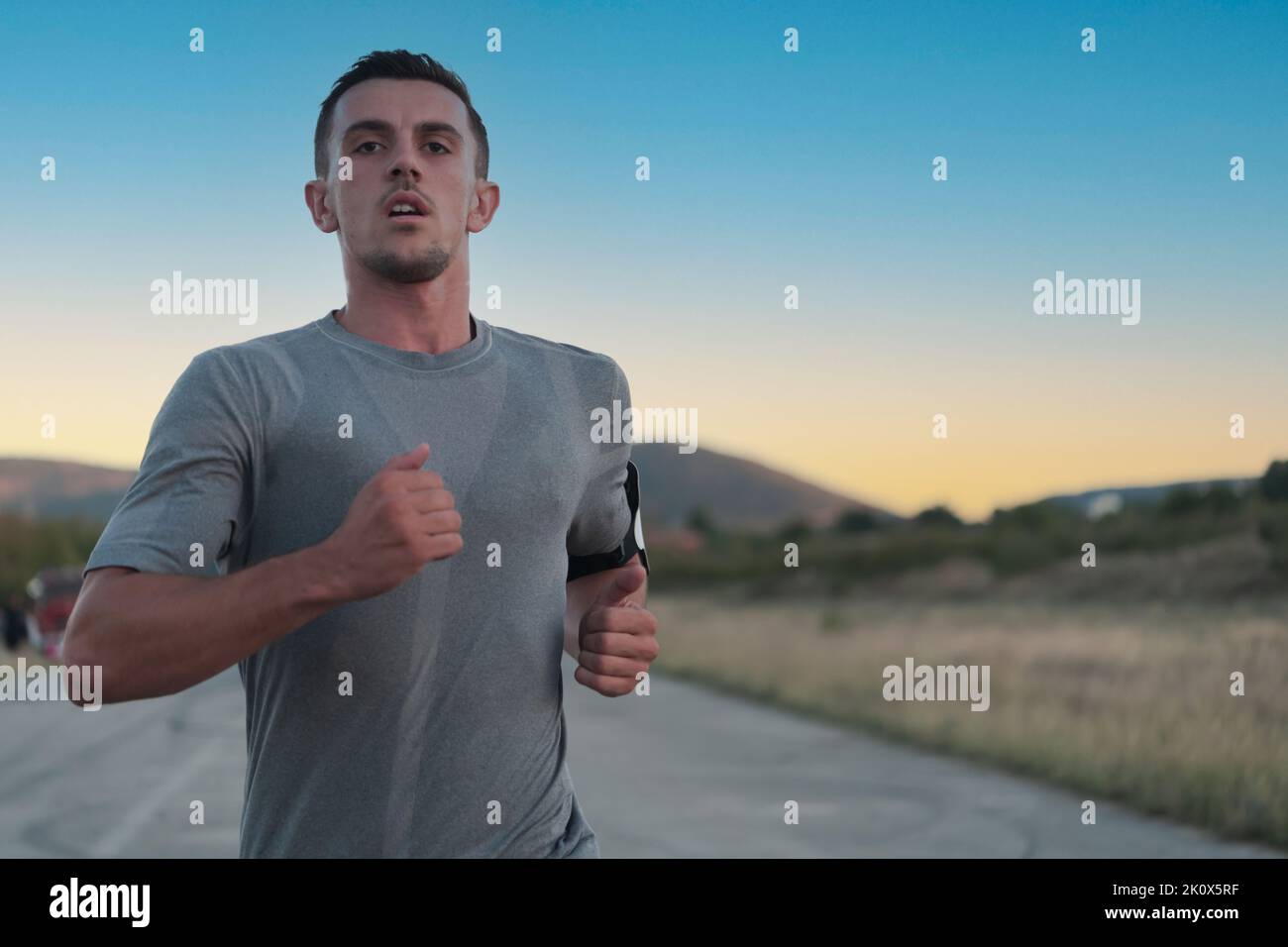 Attractive fit man running fast along countryside road at sunset light ...