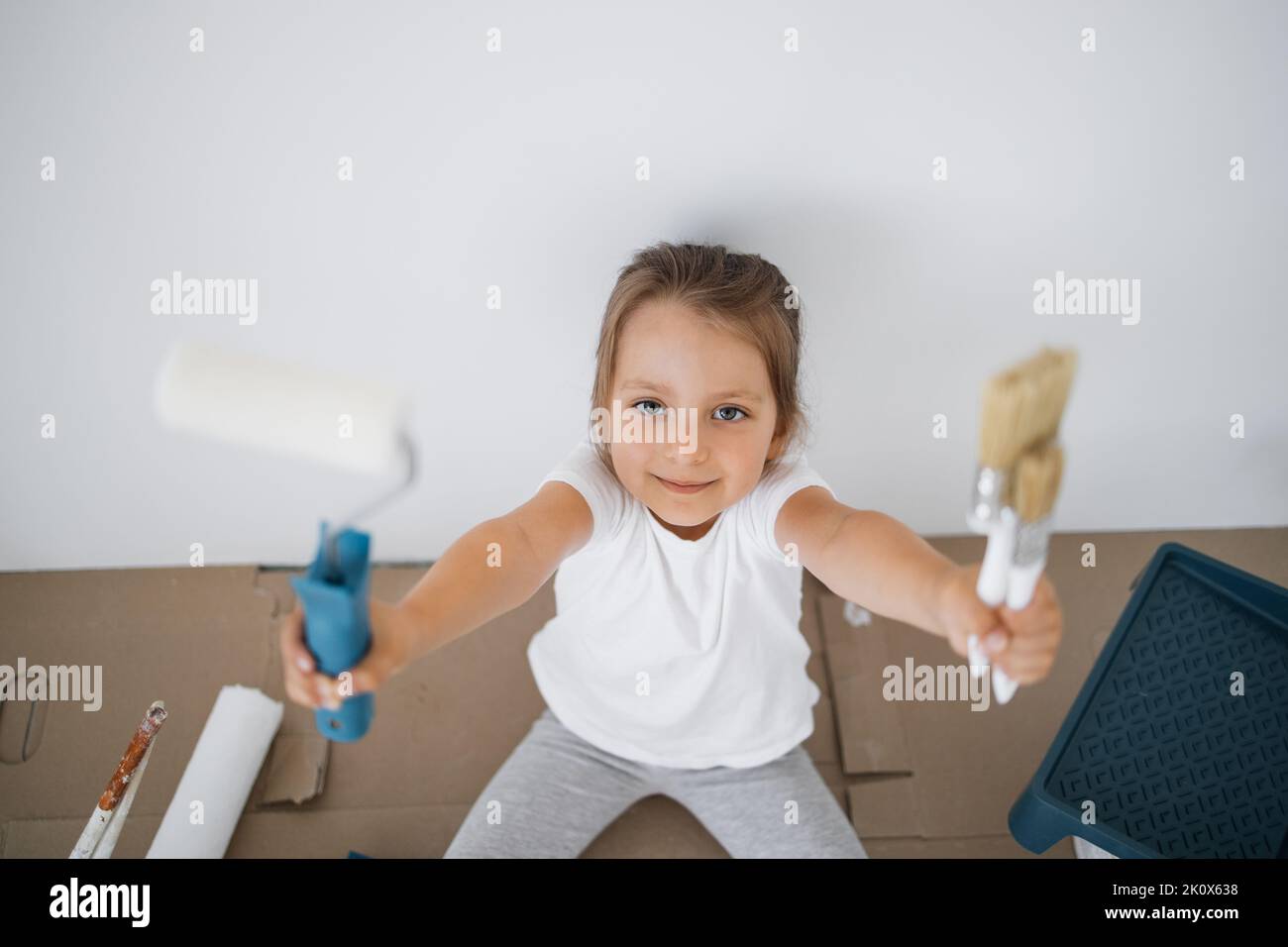 Cute little girl sitting on floor in white light room background with ...
