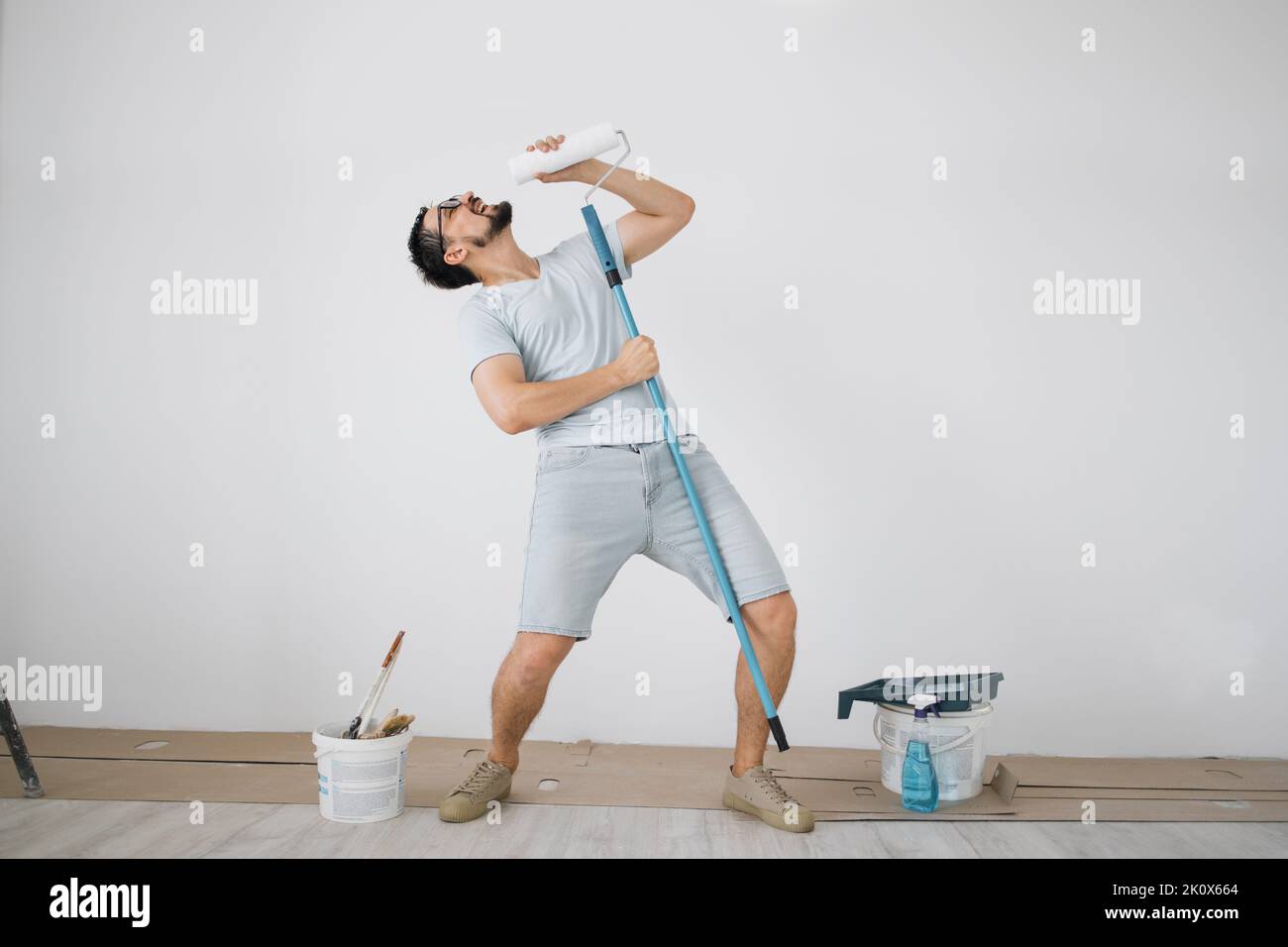 Happy caucasian male singing song using roller brush as a microphone ...