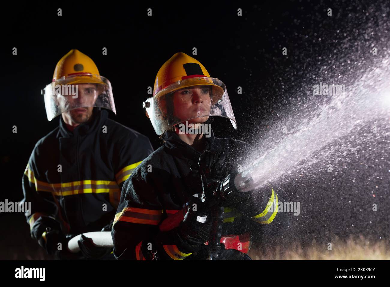 Firefighters using a water hose to eliminate a fire hazard. Team of ...