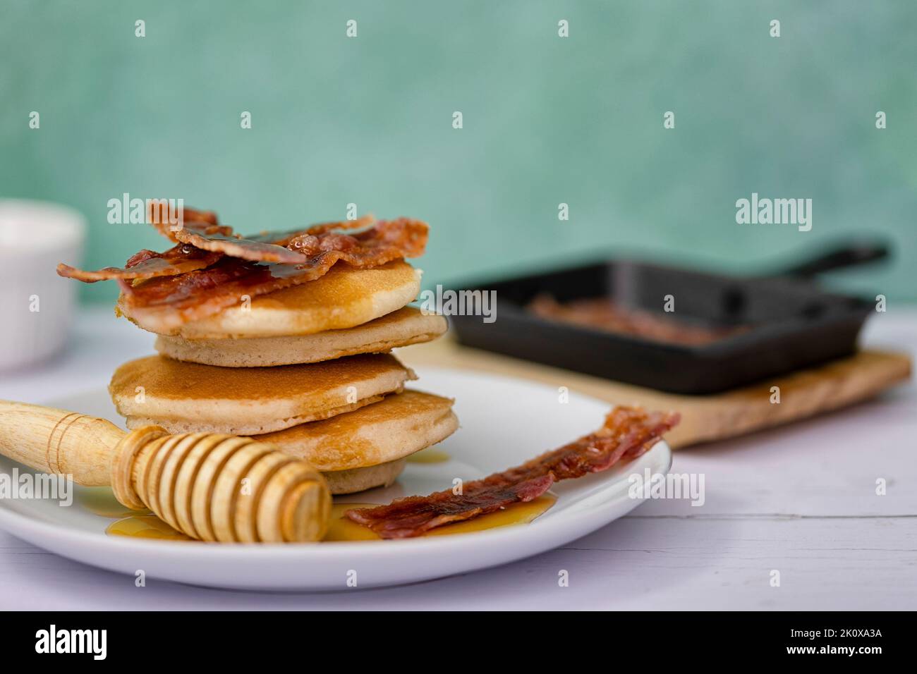 Stack of small pancakes topped with crispy bacon and honey with dipper ...