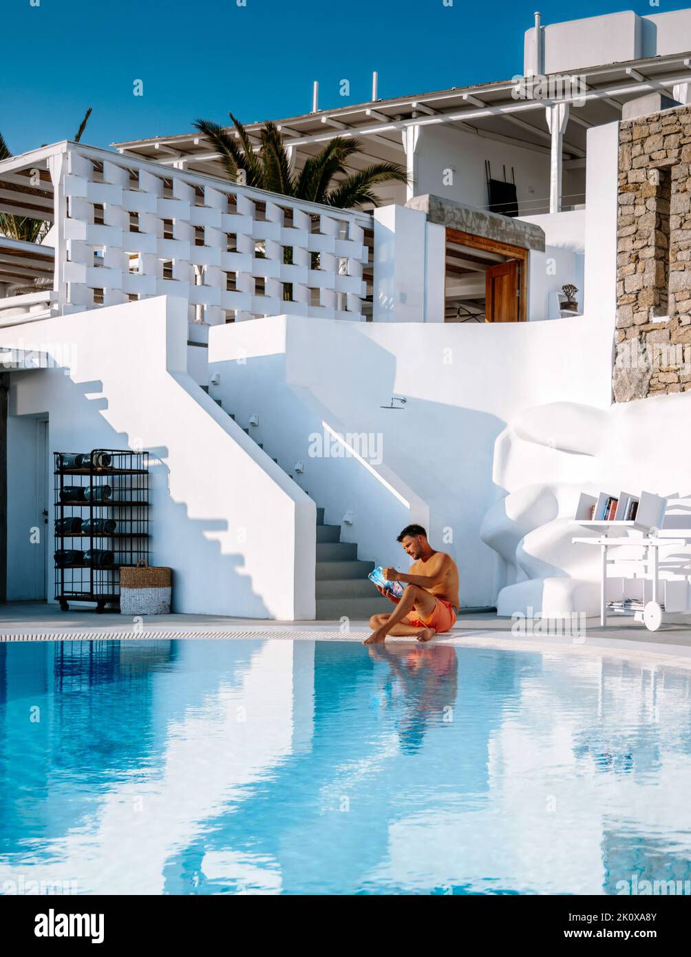 young men in swimming shorts reading a book by the swimming pool ...