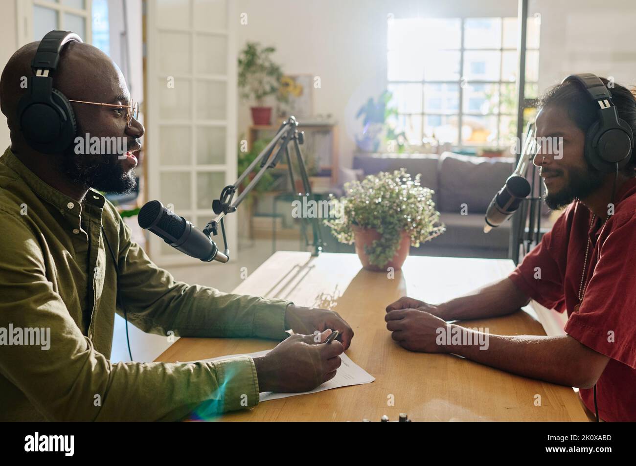Side view of two young intercultural men sitting by desk in front of ...