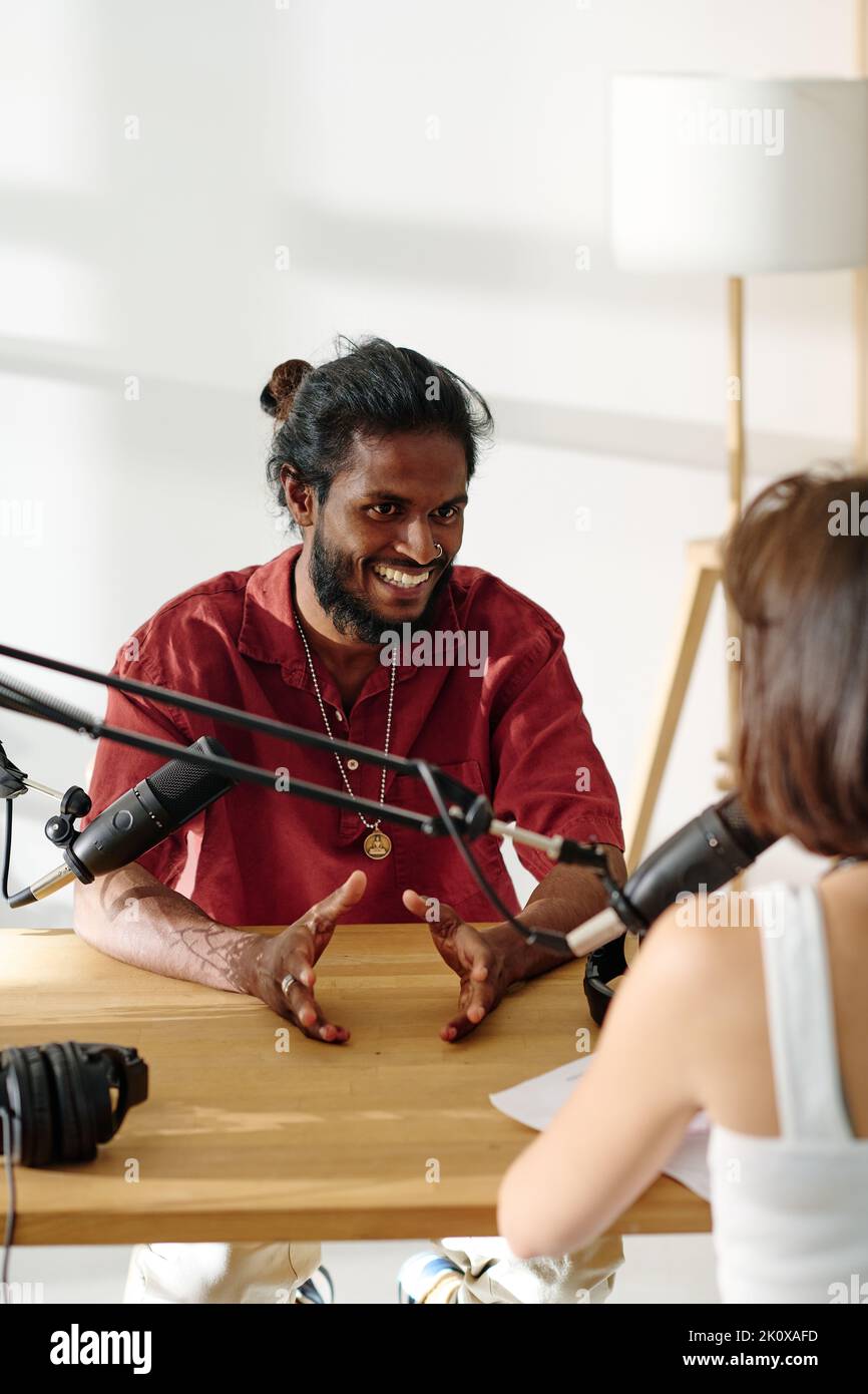 Young cheerful male host talking to invited guest while sitting in ...