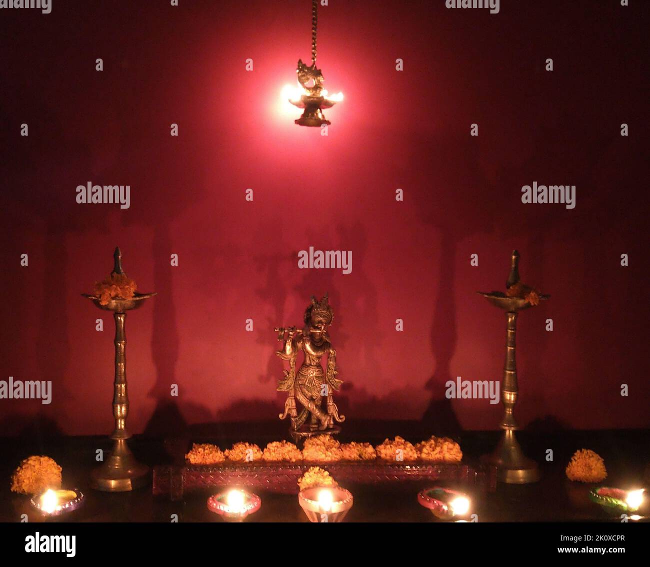 Brass idol of Lord Krishna decorated with lit clay diyas' and marigold ...