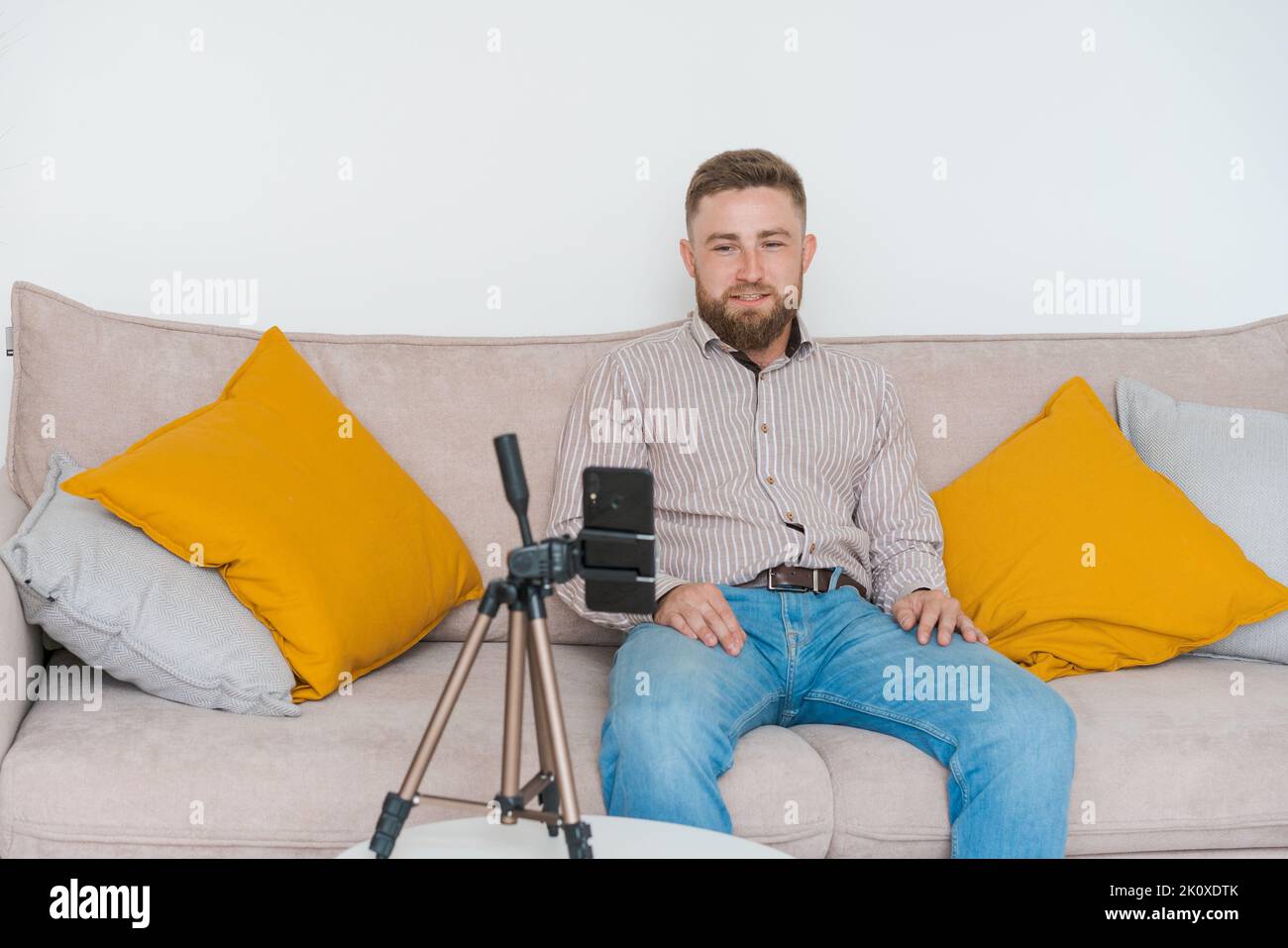 Smiling bearded guy filming video using smartphone on tripod online ...