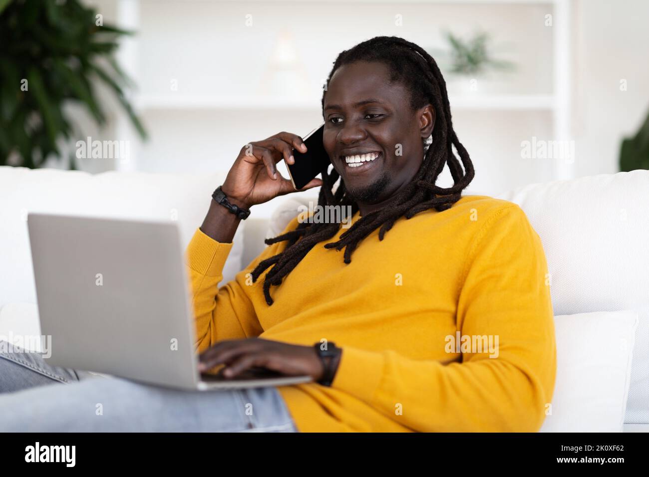 Happy Young African American Man Using Laptop And Talking On Mobile ...