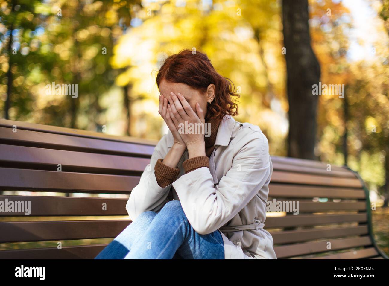 Despaired caucasian millennial red-haired lady in raincoat sits on ...