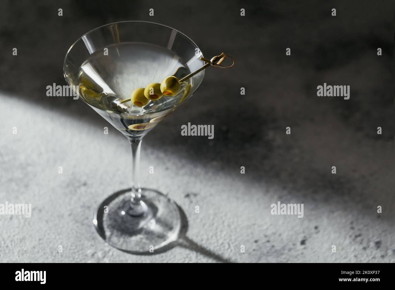 Glass of classic dry martini cocktail with olives on grey stone ...