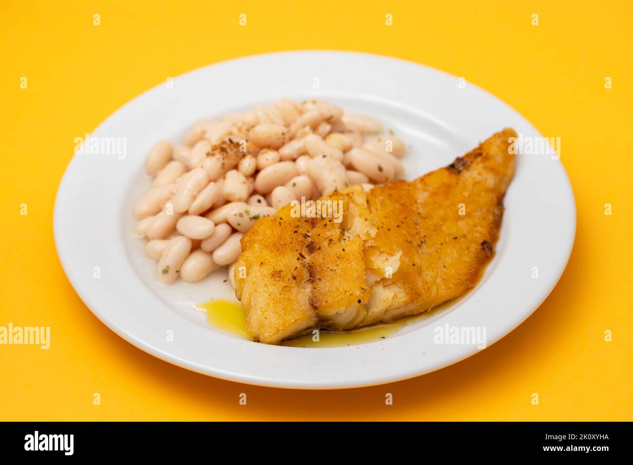 Fried cod fish with white beans on the plate on yellow paper Stock ...