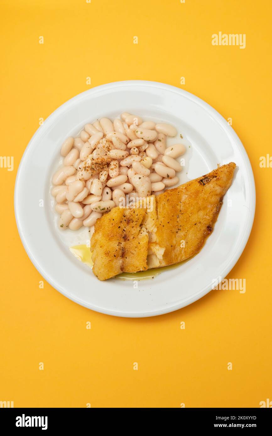 Fried cod fish with white beans on the plate on yellow paper Stock ...