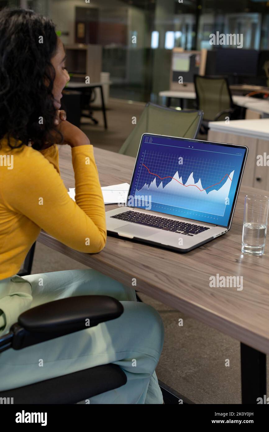 Vertical image of biracial businesswoman using laptop in empty office ...