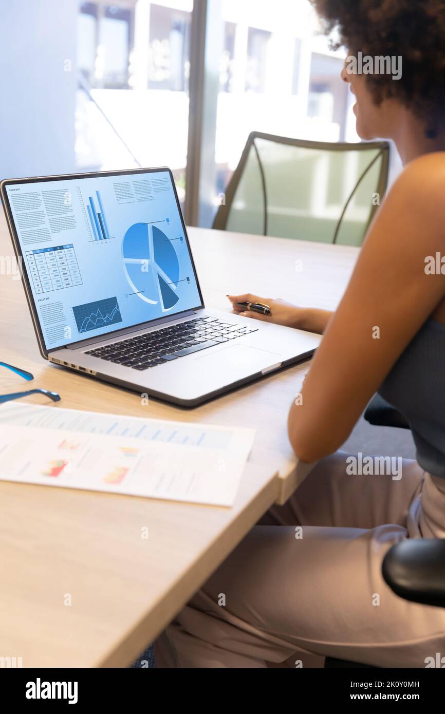 Vertical image of smiling biracial businesswoman using laptop with ...