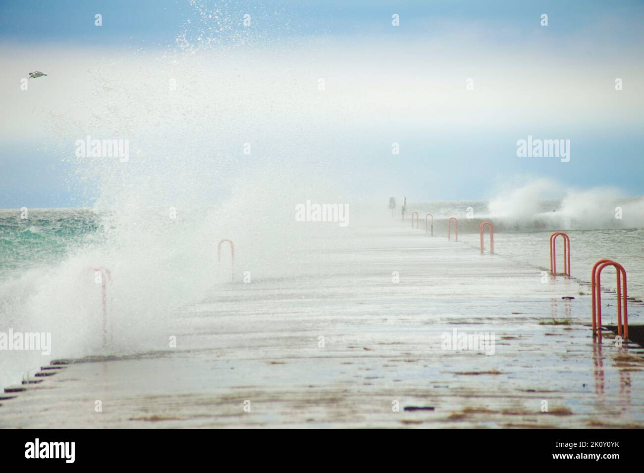 A scenic view of sea waves crashing over a wooden pier in Northern ...