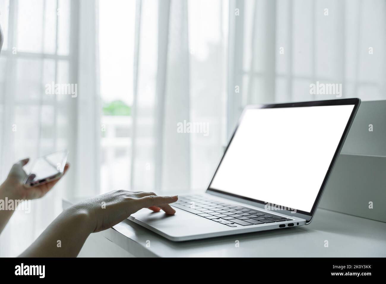 Woman hands using laptop with blank screen on white table at home or ...