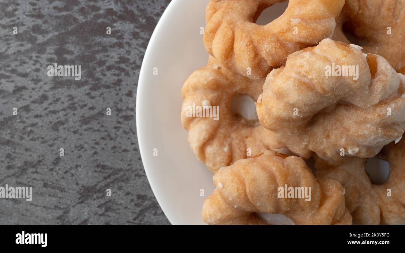Top close view of cruller shaped donuts on a white plate atop a mottled ...
