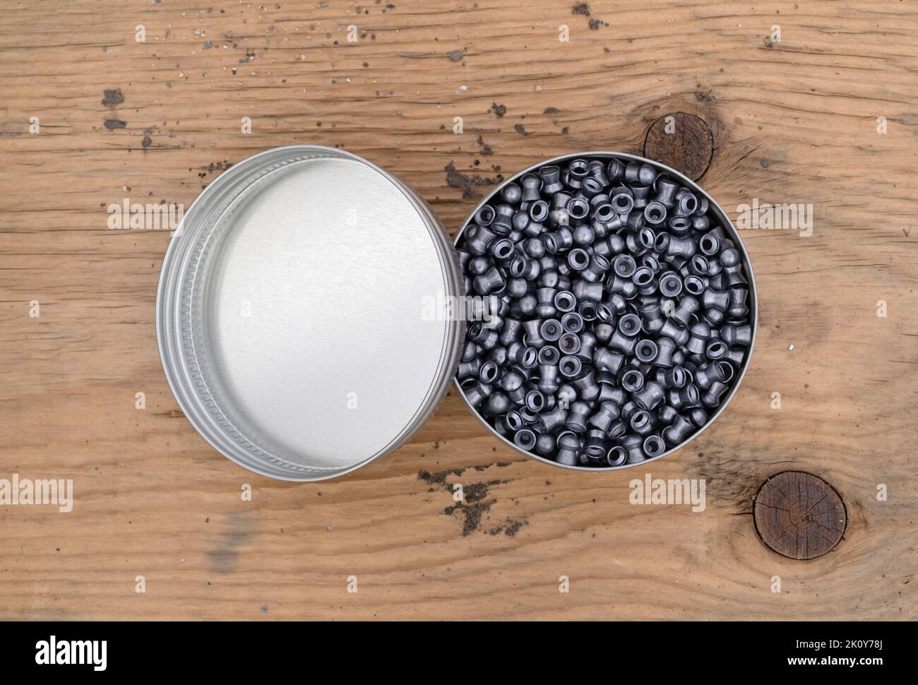 Top close view of an open tin of air gun pellets on a wood board ...