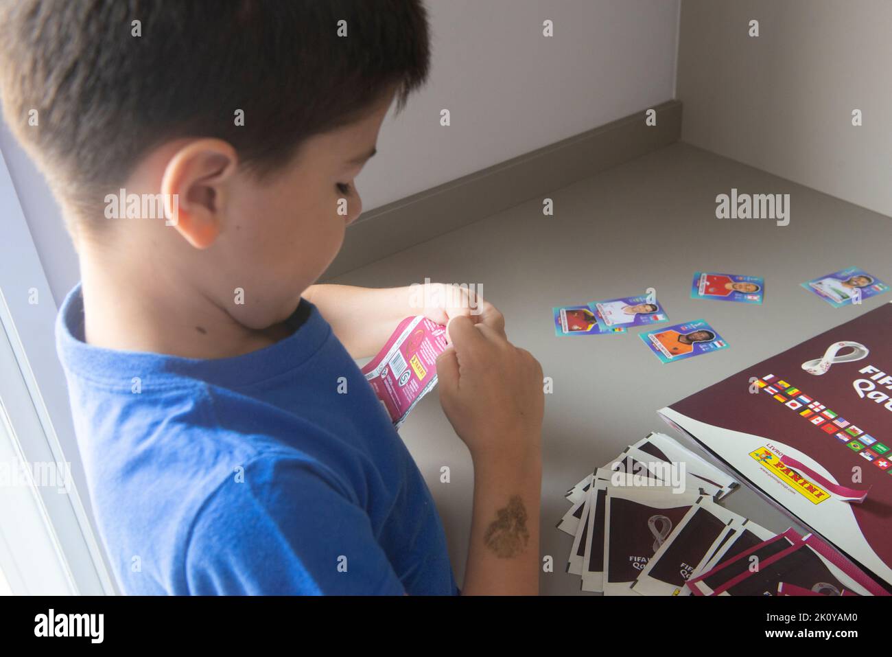 Bauru, Brazil - 12.09.22: Back view of boy opening sticker packs to ...