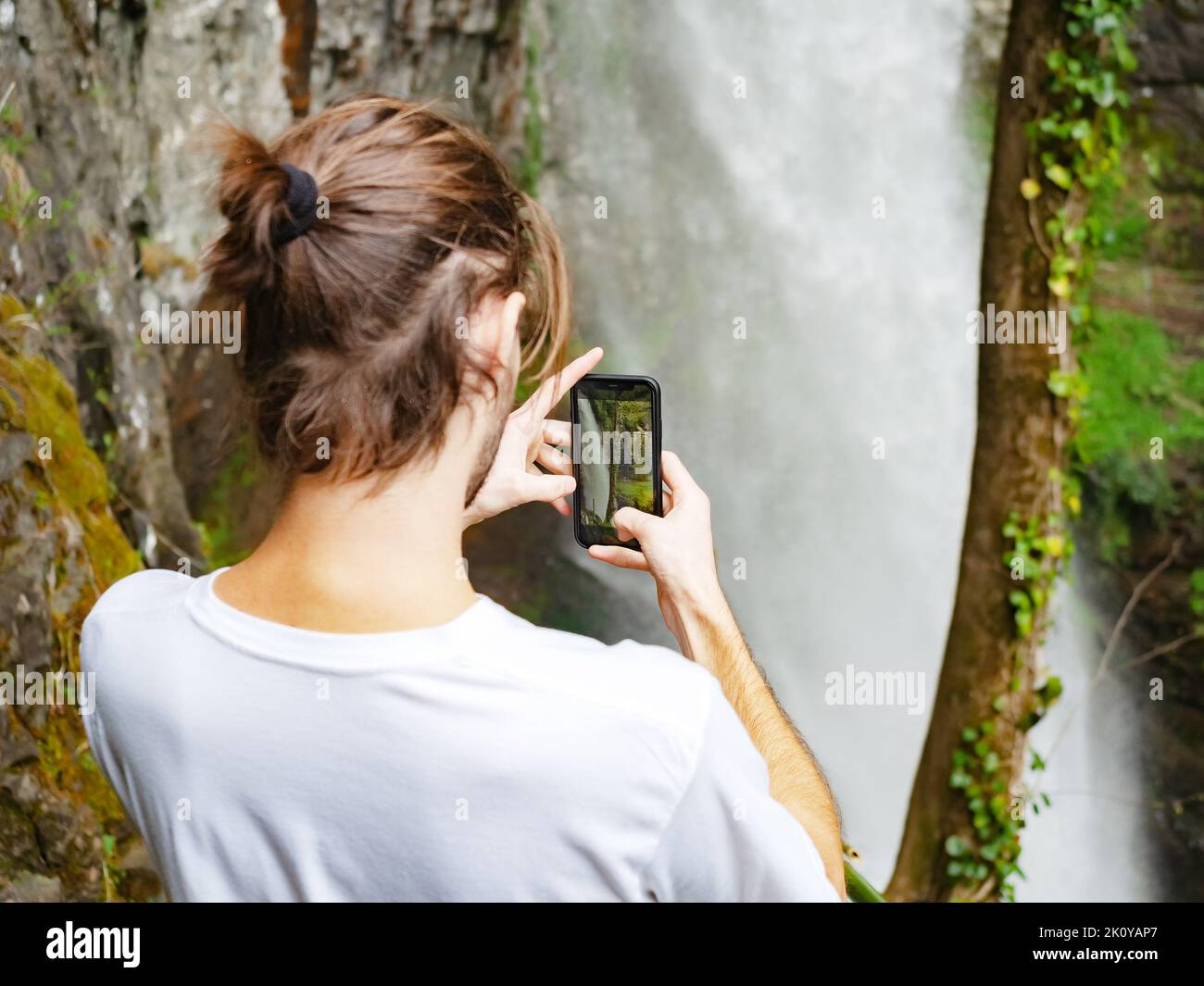 A young man photographs a waterfall in a high rocky gorge on his phone ...