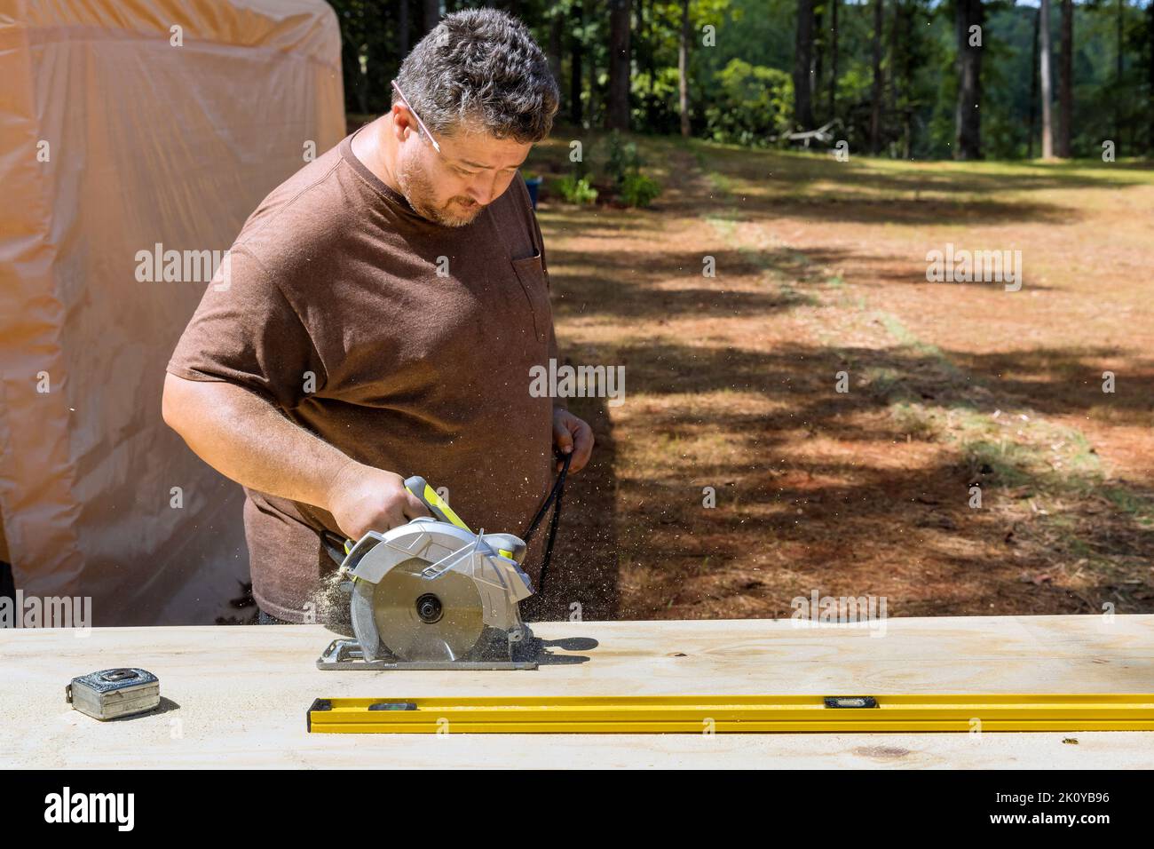 The worker holds a circular saw in his hand while cutting plywood with ...