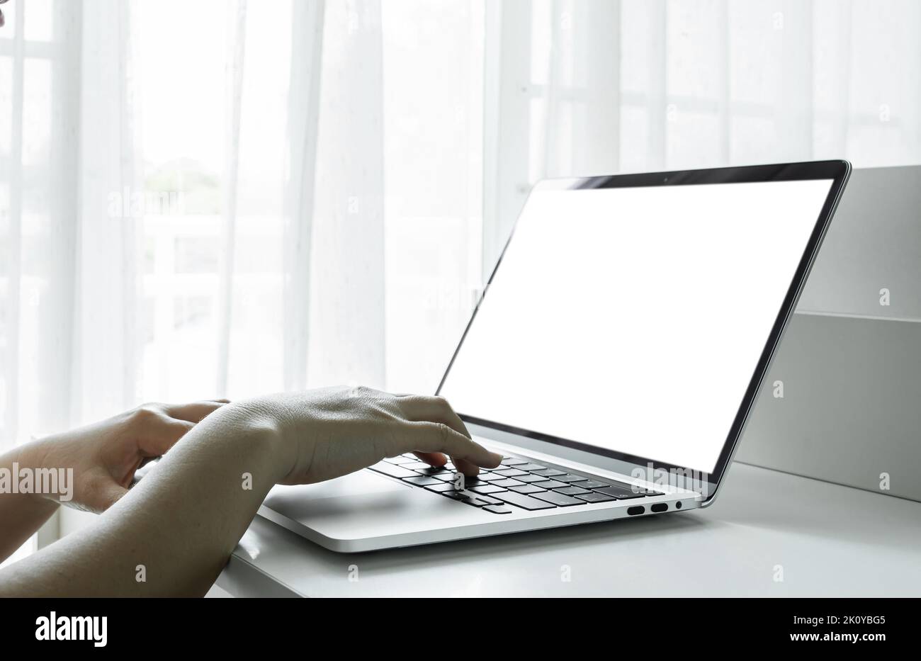 Woman hands using laptop with blank screen on white table at home or ...