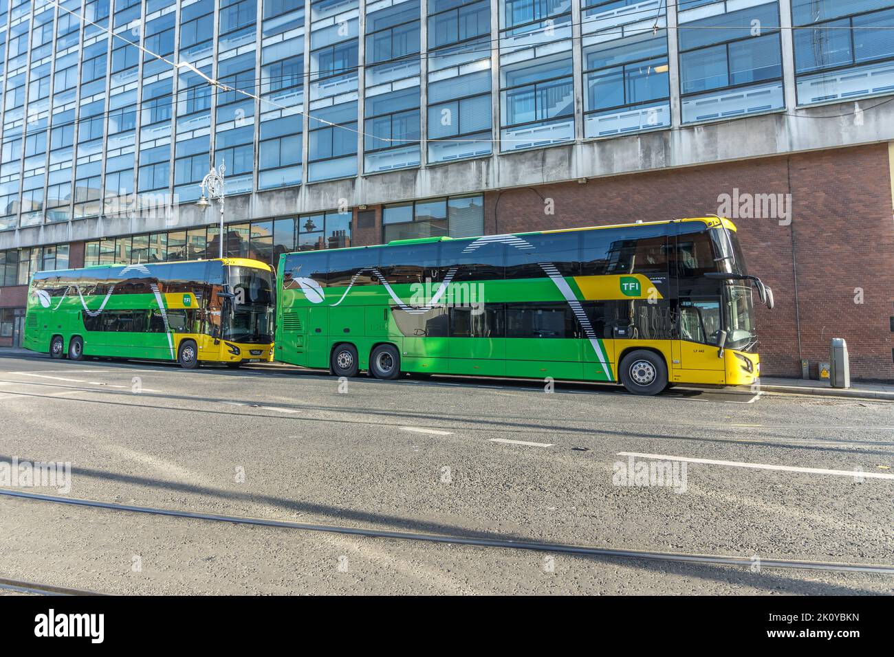 Two parked green and yellow double-deck buses and a glass building in ...