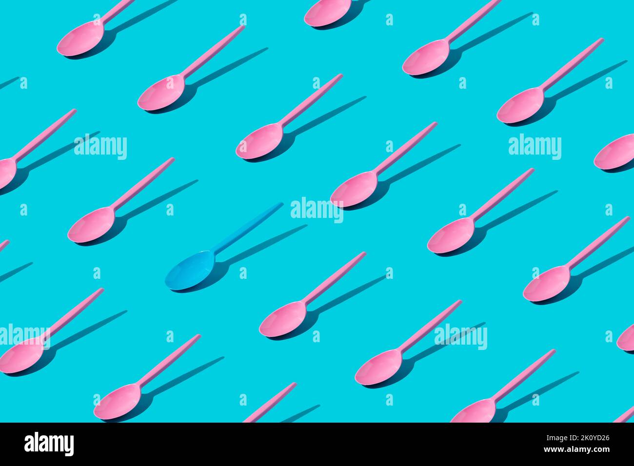 Pattern made of pink plastic spoons and one blue plastic spoon on blue ...
