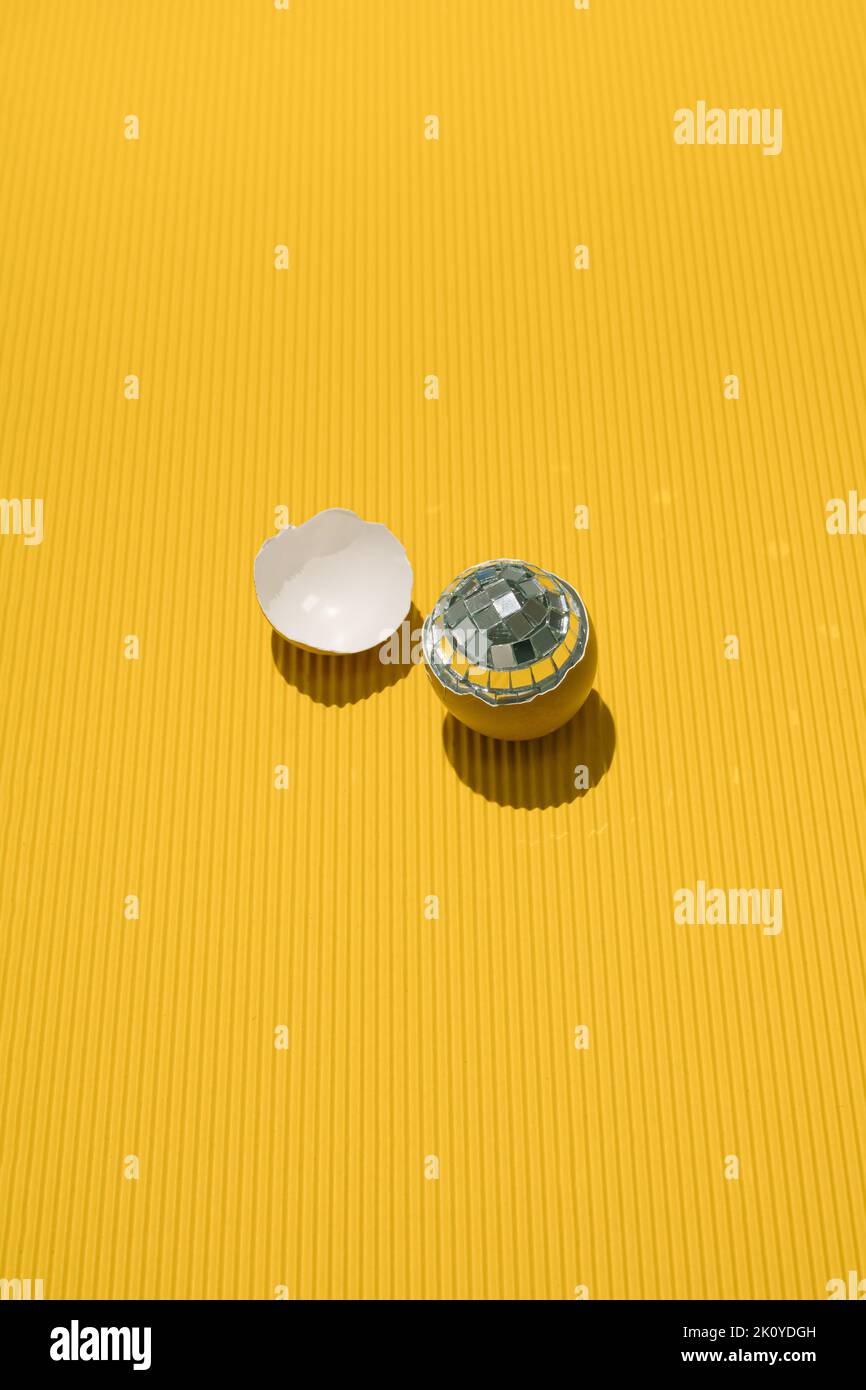 Disco ball in a cracked egg shell on yellow background. Minimal concept ...