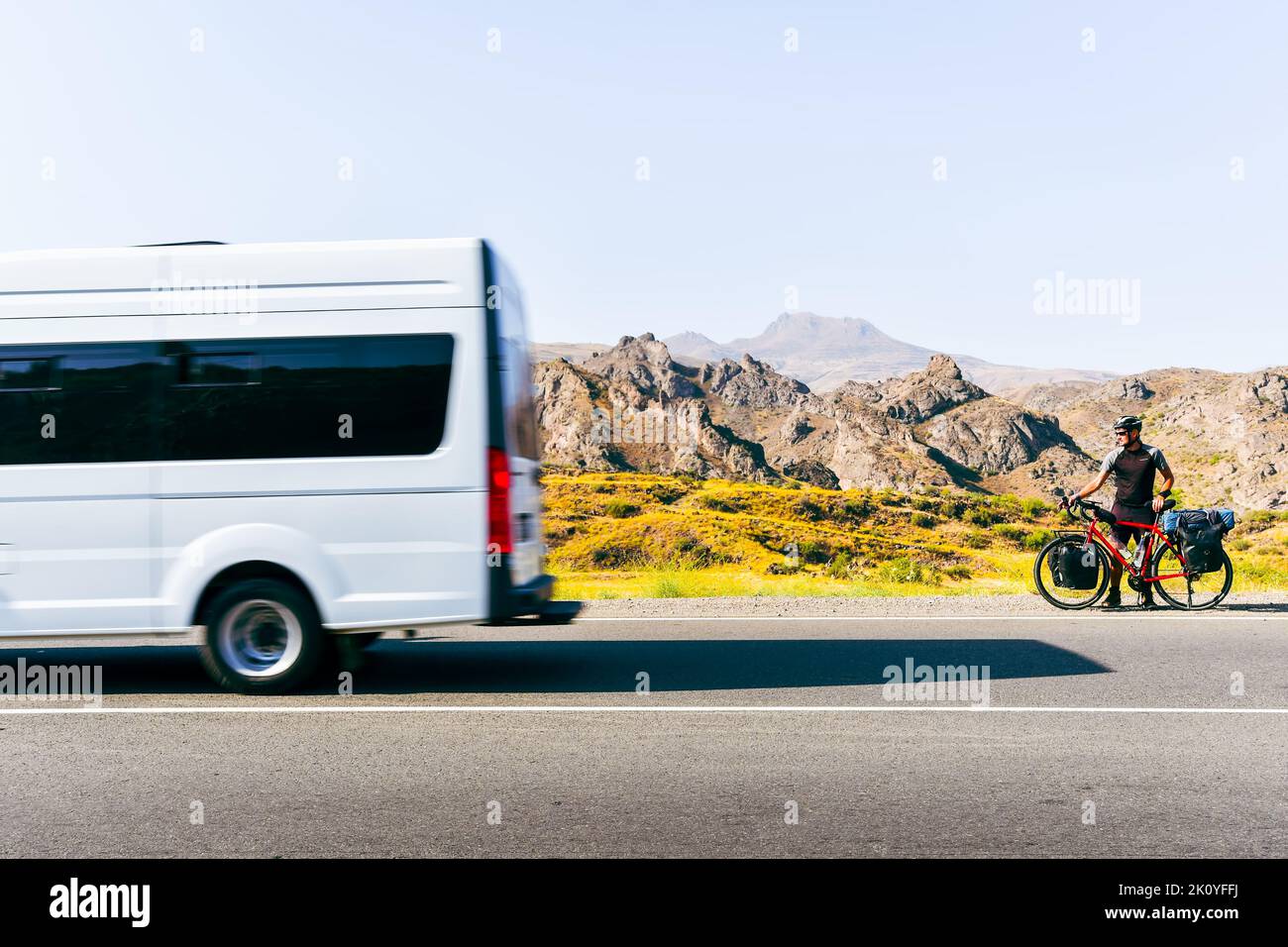 Road side view white van pass male cyclist on side of road in Armenia ...