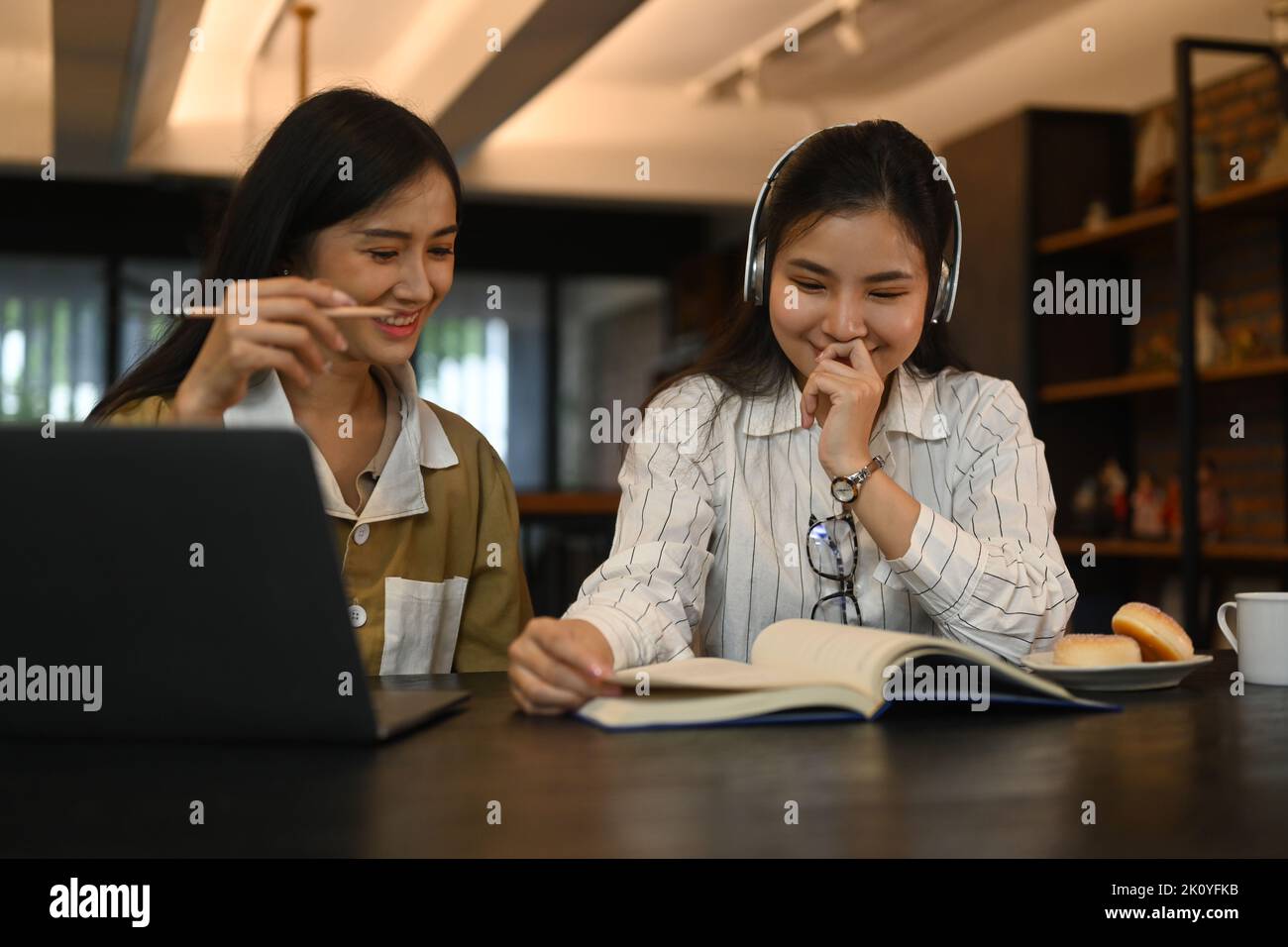 Two cheerful young students reading book while preparing for exams in ...