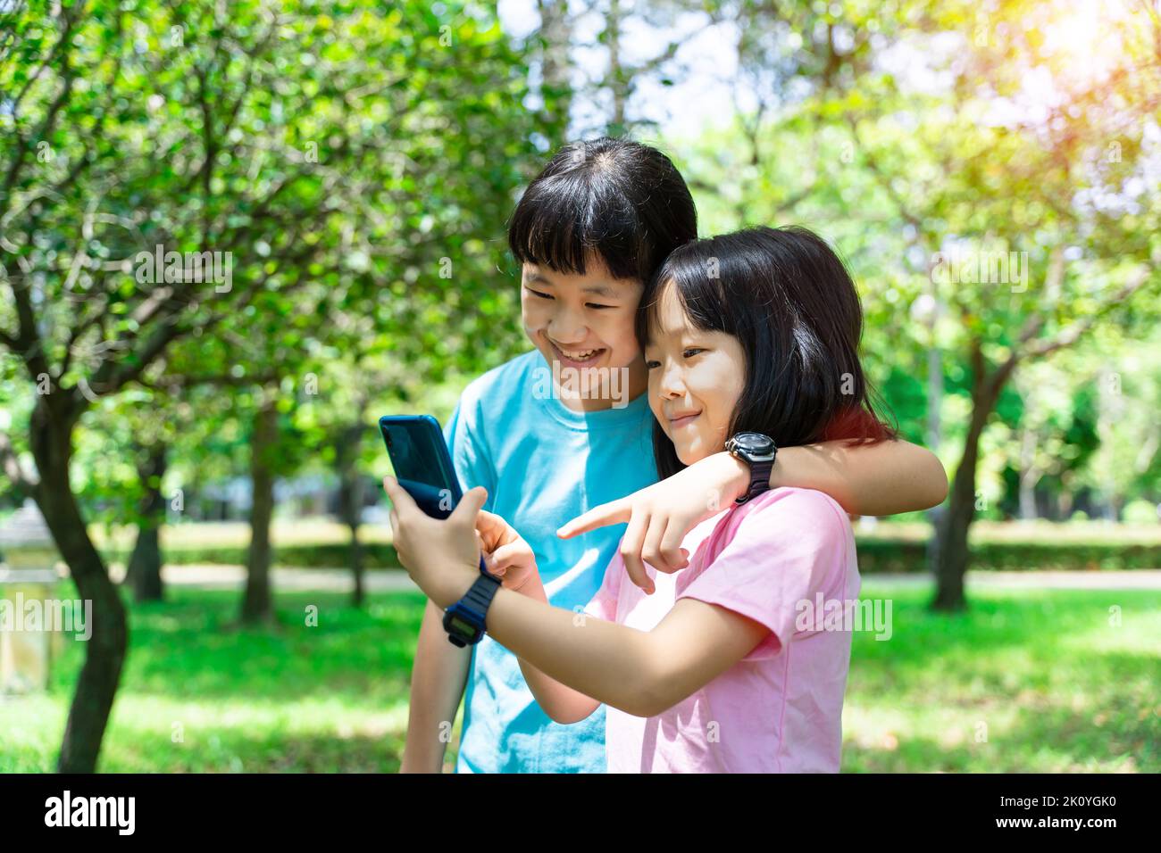 Two sisters hugging while using mobile phone in the park. Happy family ...