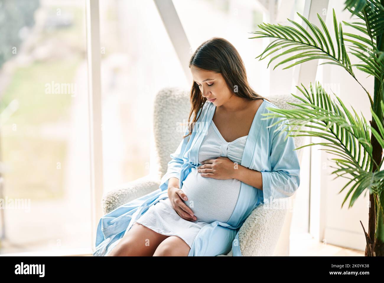 Pregnant happy woman touching her belly rest on chair at modern home ...